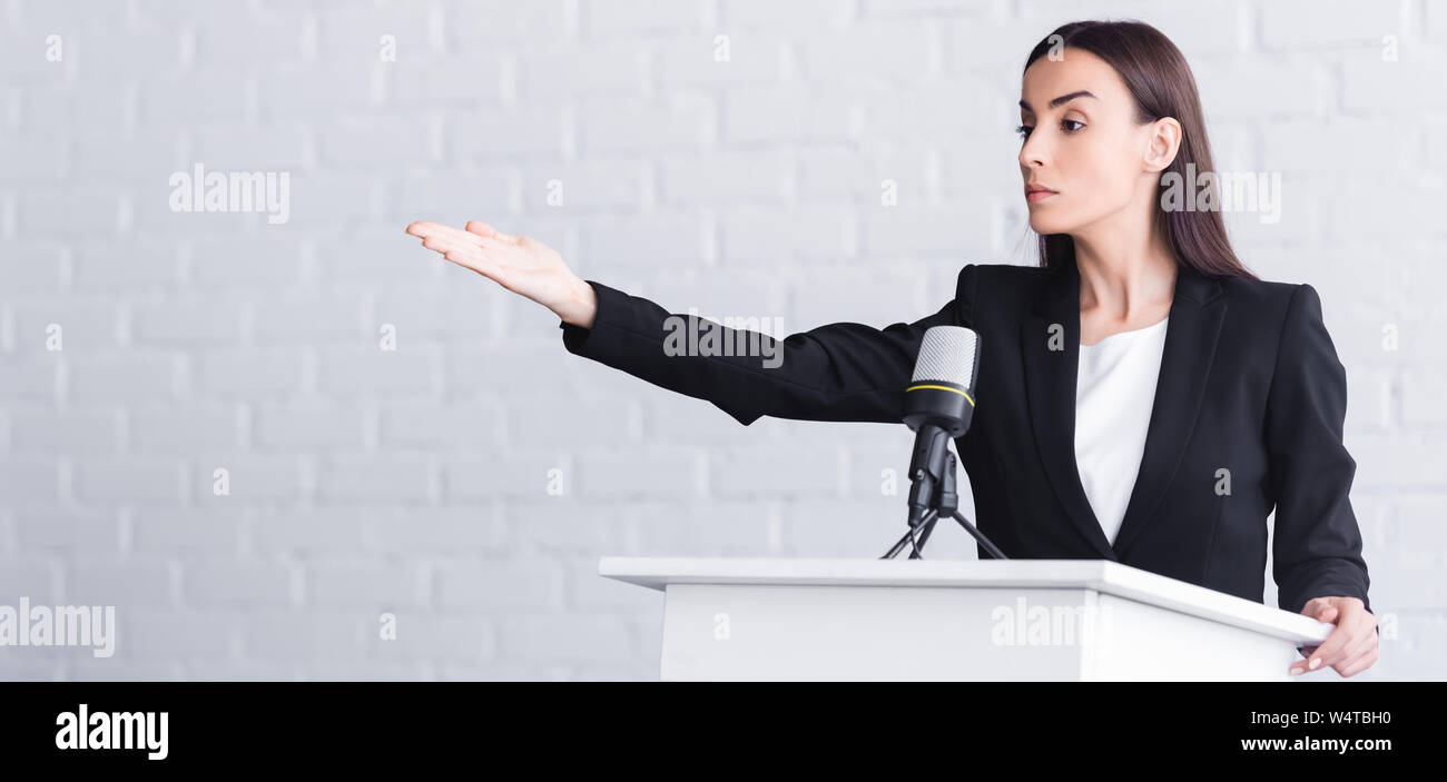 panoramic shot of beautiful, serious lecturer pointing with hand while ...
