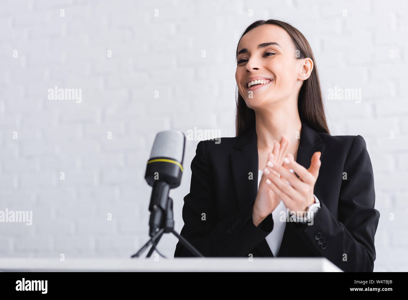 beautiful, happy lecturer clapping hands while standing on podium ...