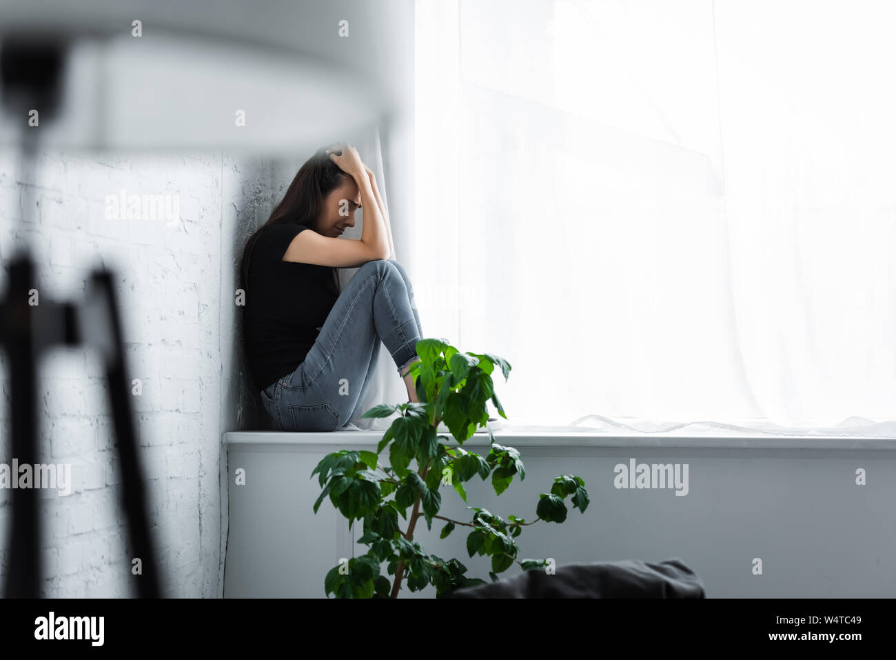 selective focus of depressed young woman crying while sitting on window ...