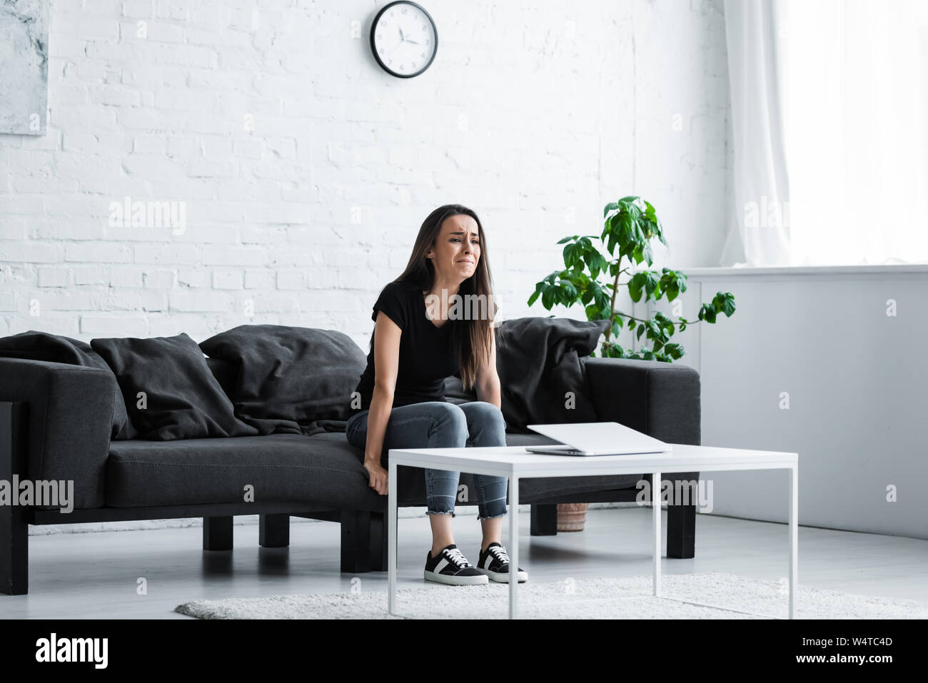 crying woman sitting on sofa at home while suffering from depression ...