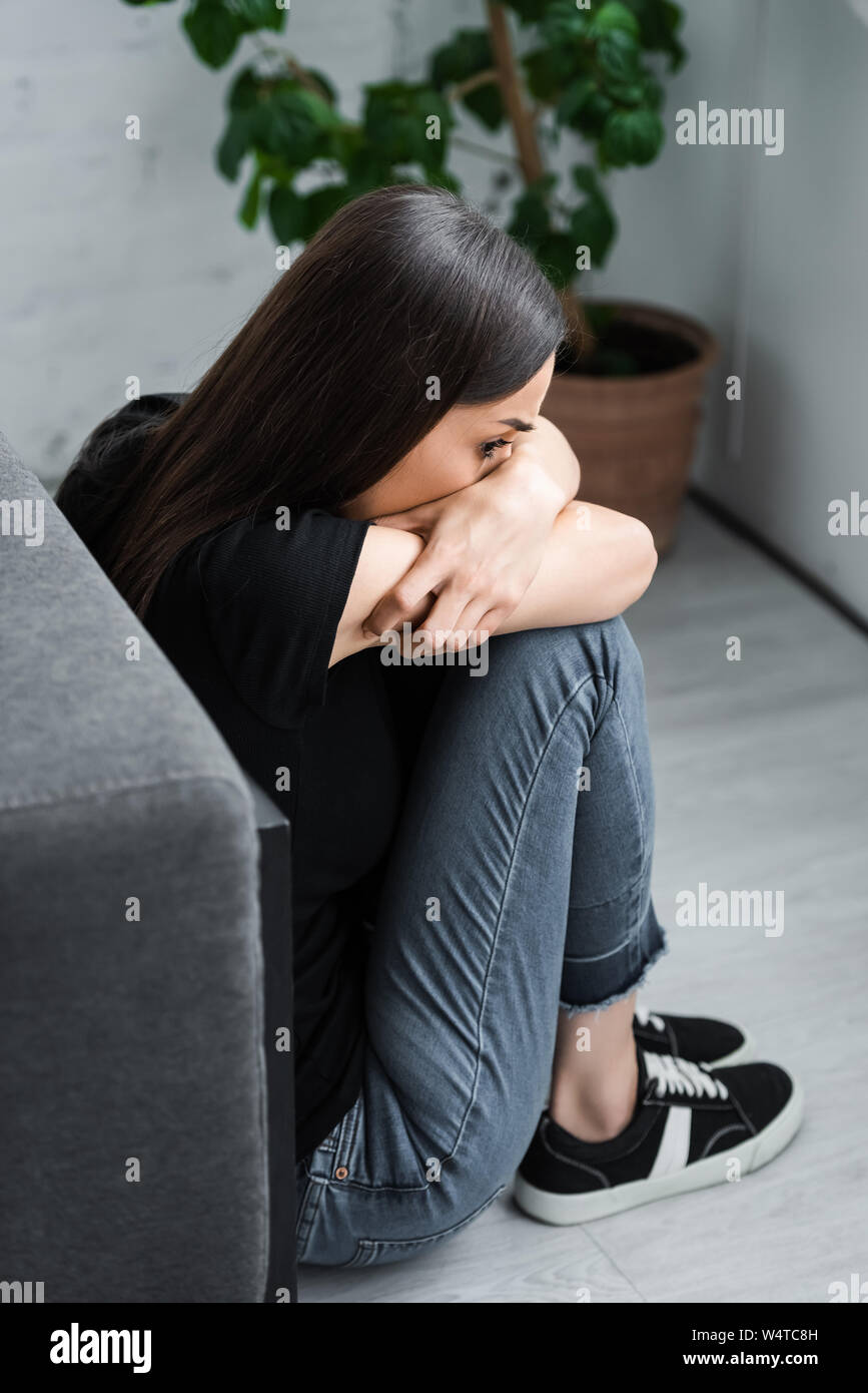scared young woman hiding face in crossed arms while sitting on floor ...