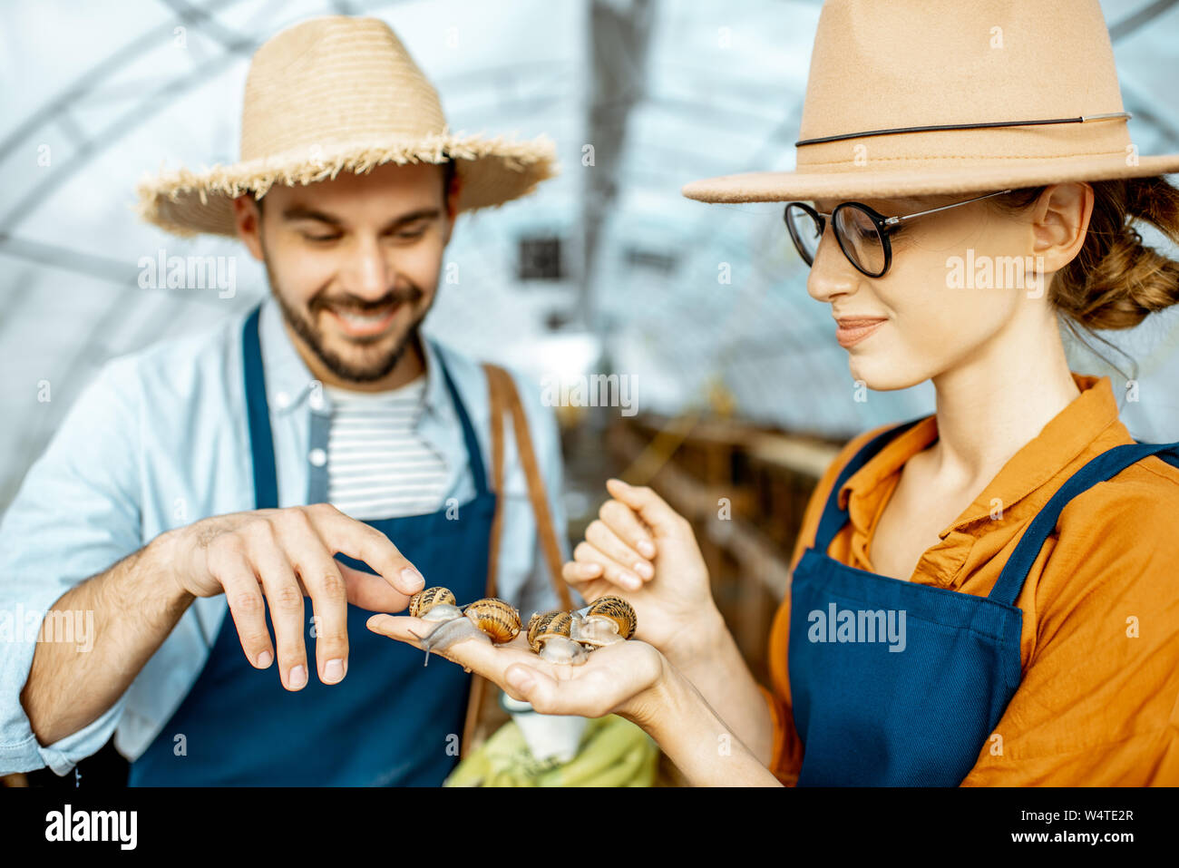 Two young beautifully dressed farmers examining snails growing process ...