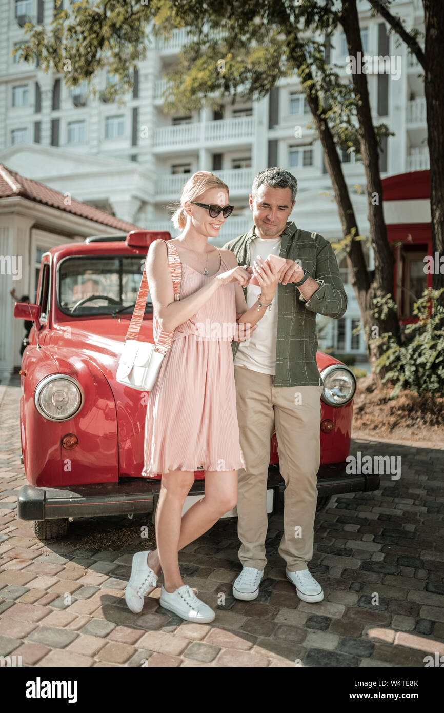 Scrolling together. Cheerful married couple standing outside near their ...