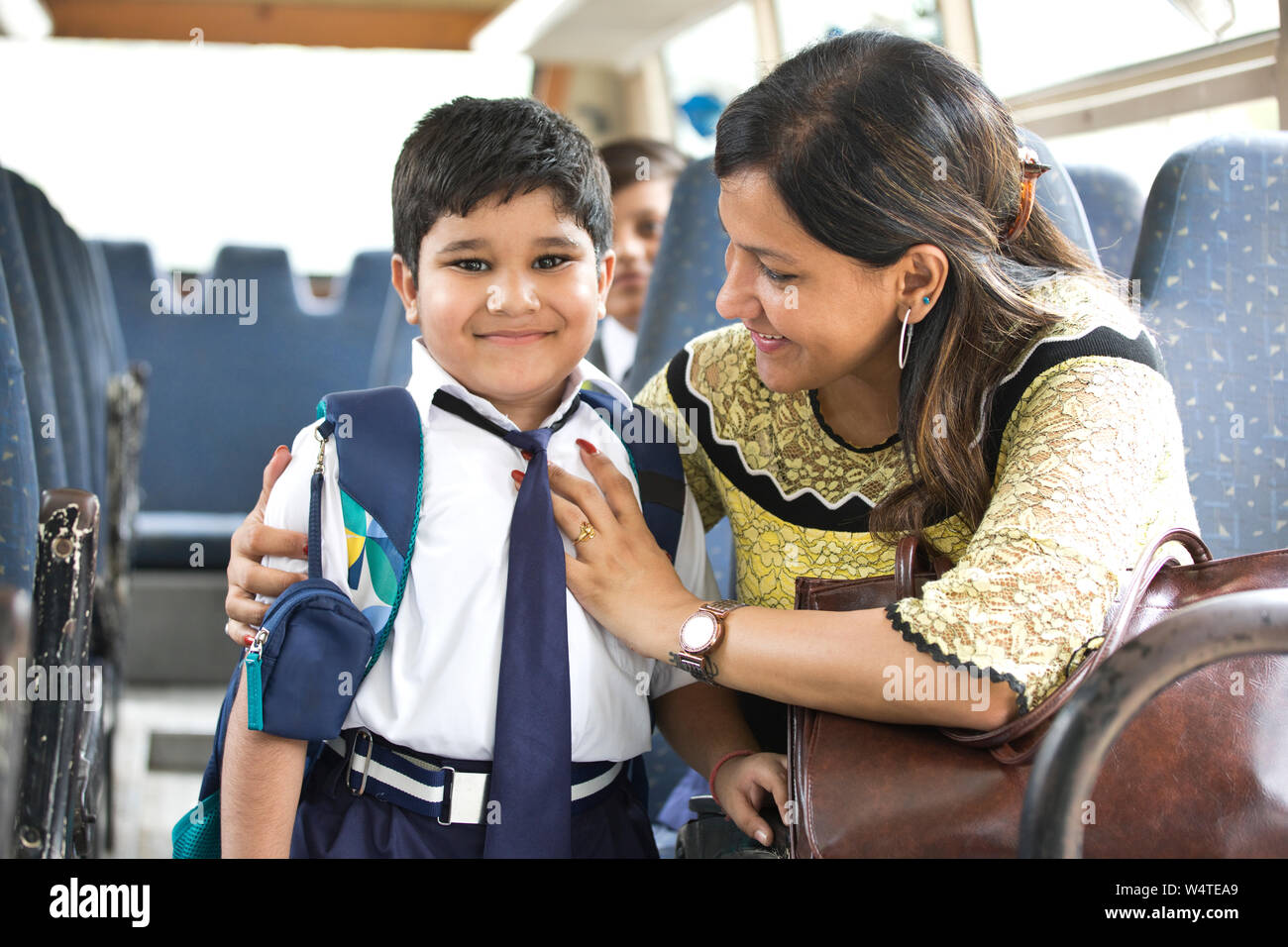 Happy teacher taking care of schoolboy while traveling in school bus ...