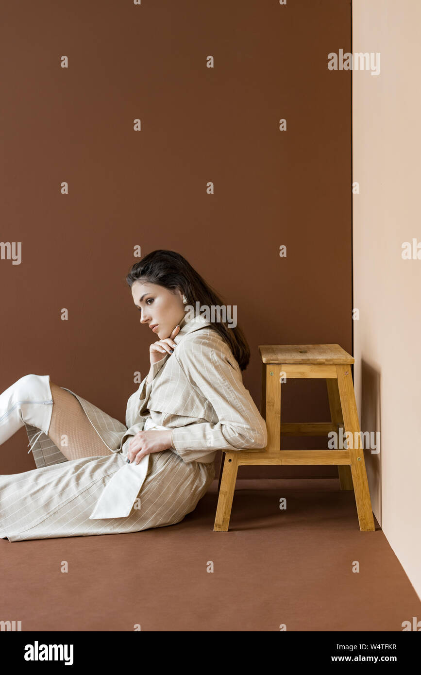 side view of stylish model in beige trench coat sitting on floor ...