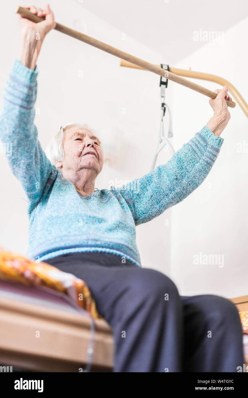 Elderly 96 years old woman exercising with a stick sitting on her bad ...