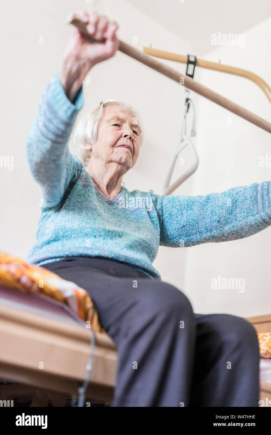 Elderly 96 years old woman exercising with a stick sitting on her bad ...