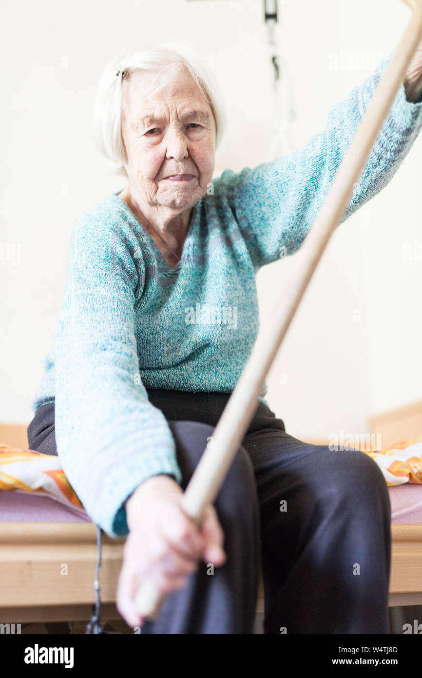 Elderly 96 years old woman exercising with a stick sitting on her bad ...