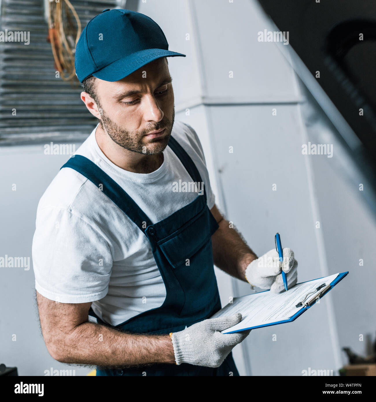selective focus of handsome repairman in cap holding pen and clipboard ...