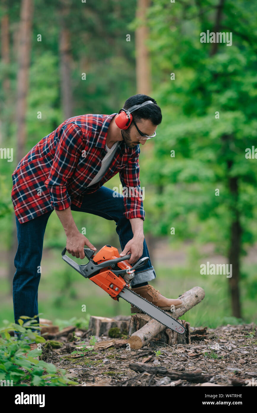 lumberer in noise-canceling headphones cutting wood with chainsaw in ...