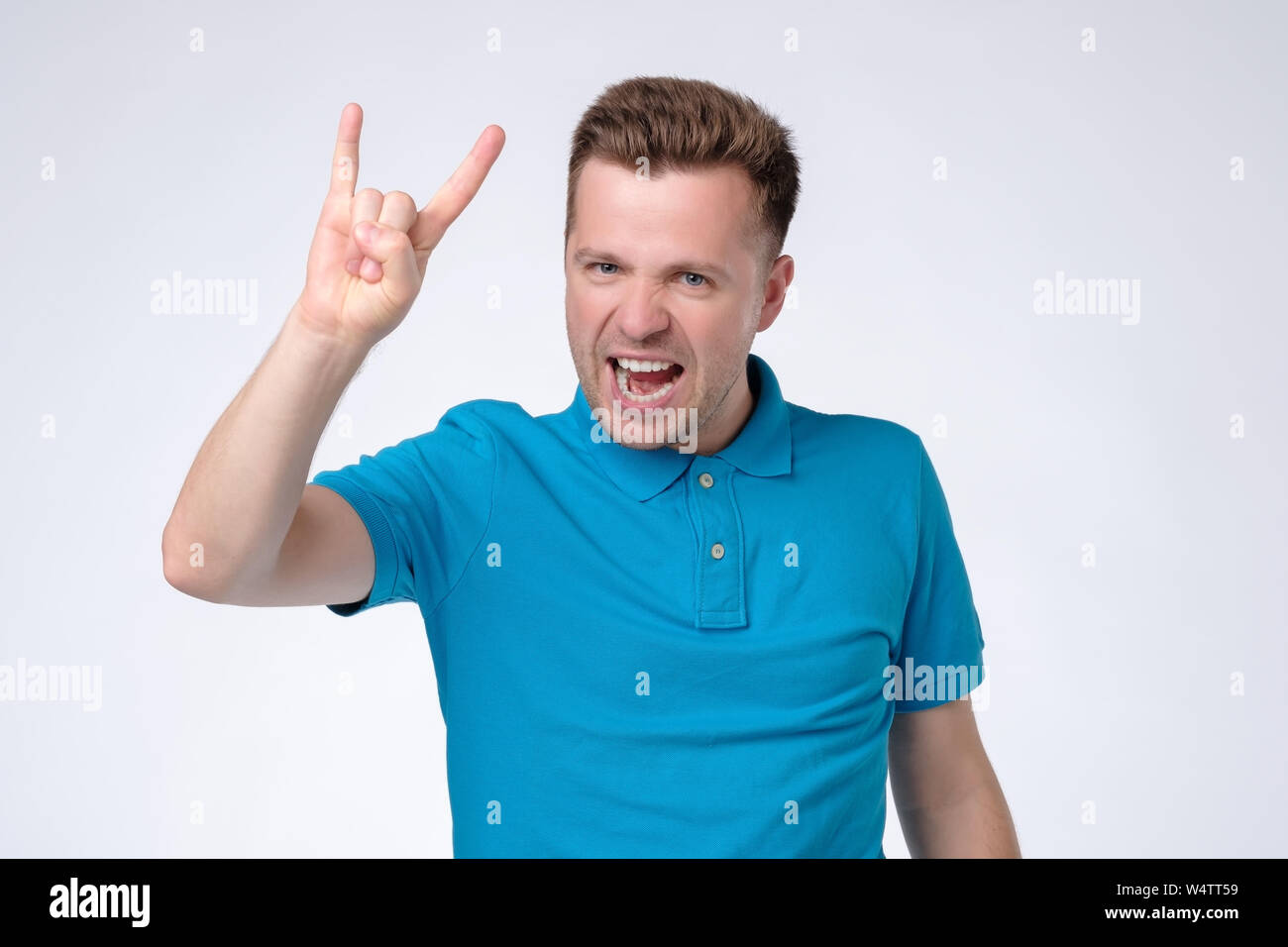 Young handsome man screaming and making rock gesture with hands while ...