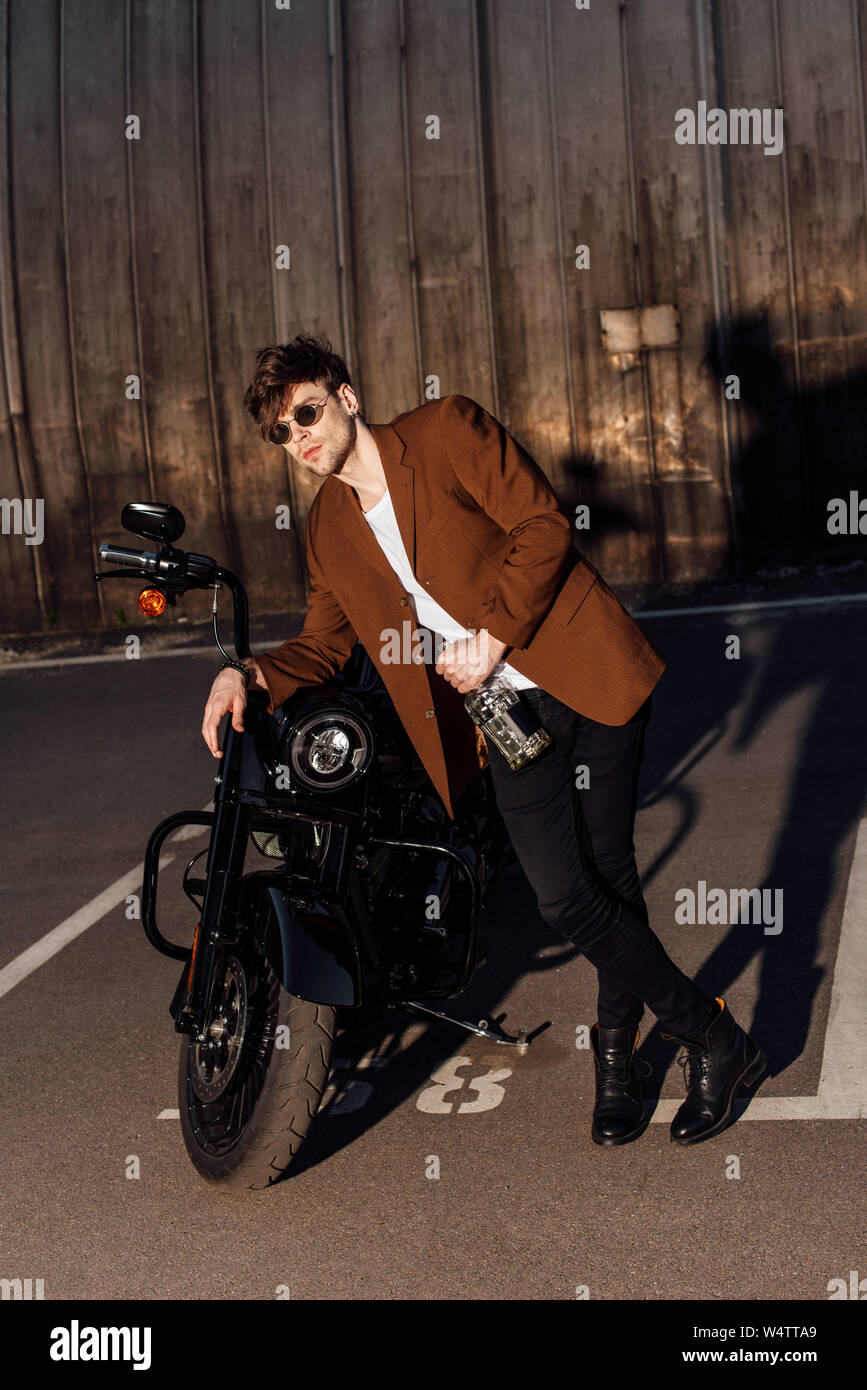 full length view of man in suit leaning on motorcycle and holding ...