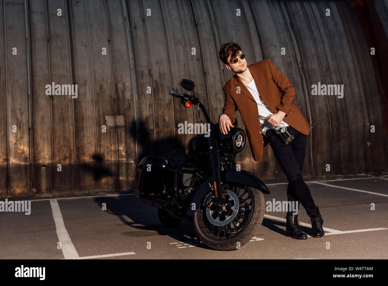 full length view of man standing in light place leaning on motorcycle ...