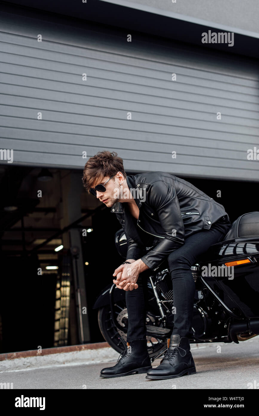full length view of handsome man sitting on motorcycle with clenched ...