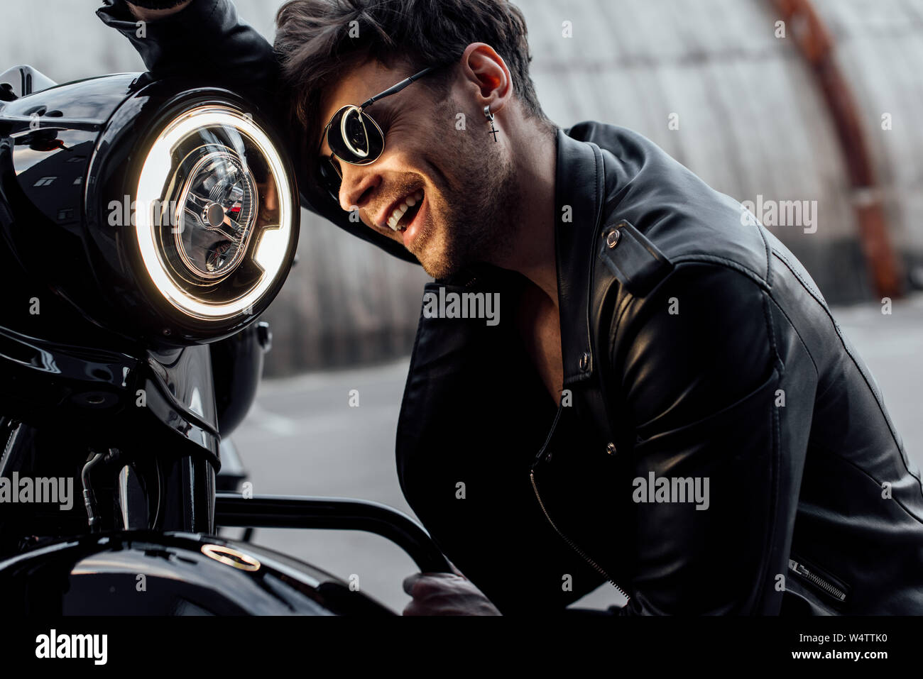 handsome young man leaning on motorcycle and smiling while looking at ...