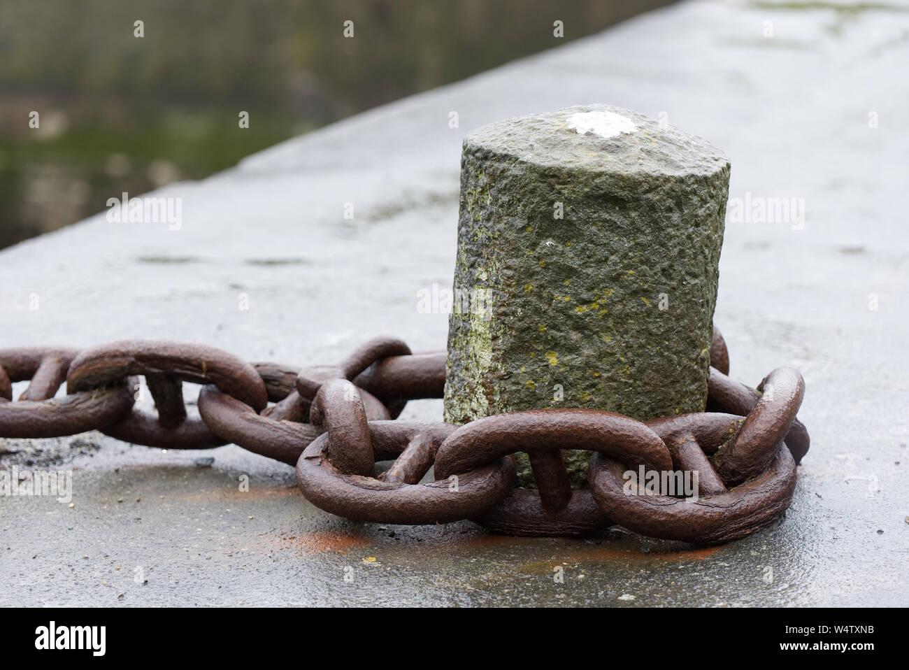 Large rusty old fishing boat chain looped around a concrete mooring on ...