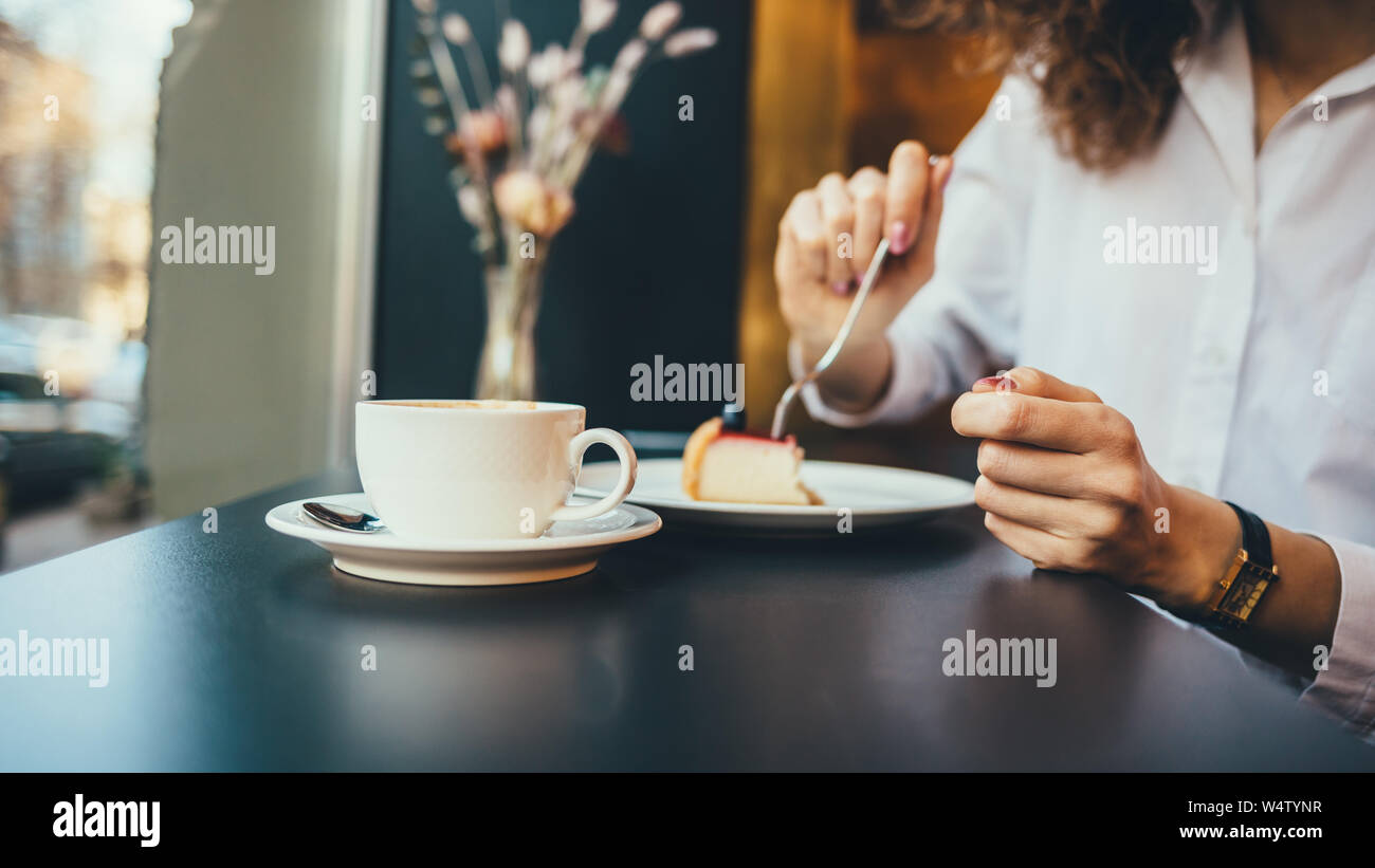 Young woman eating cheesecake and drinking coffee sitting in cafeteria ...