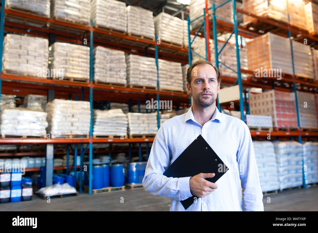 Male supervisor holding clipboard and looking away in warehouse Stock ...