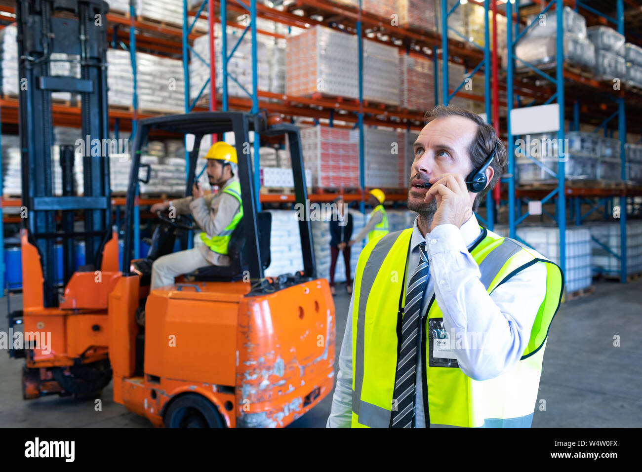 Male supervisor talking on headset in warehouse Stock Photo - Alamy