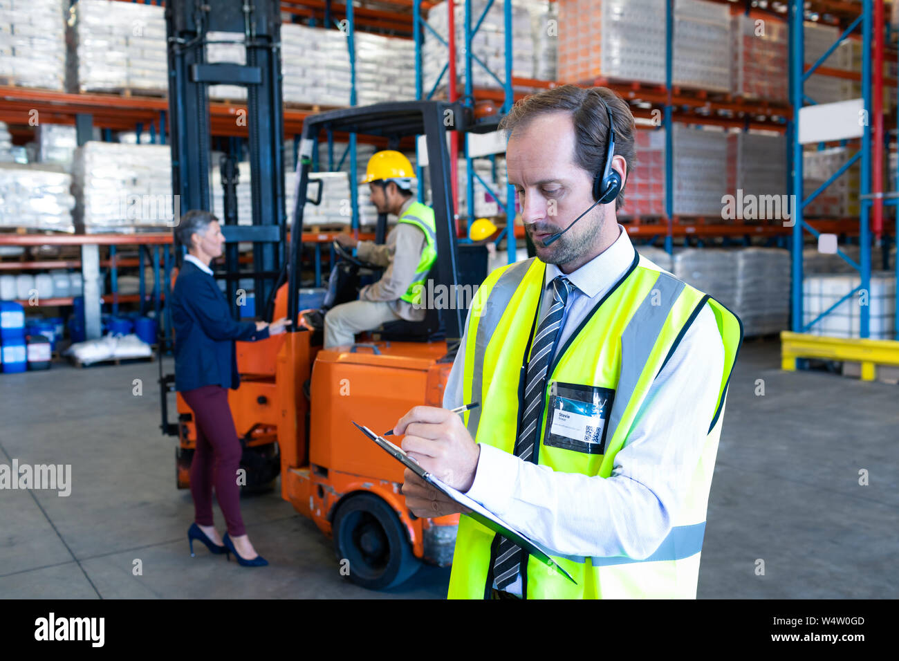 Male supervisor with headset writing on clipboard in warehouse Stock ...