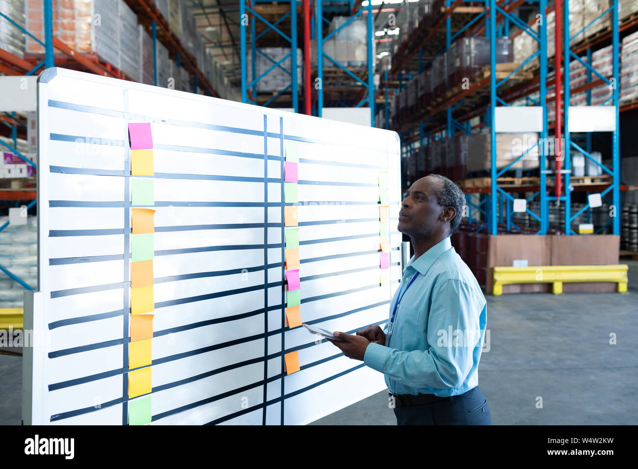Male supervisor looking at whiteboard in warehouse Stock Photo - Alamy