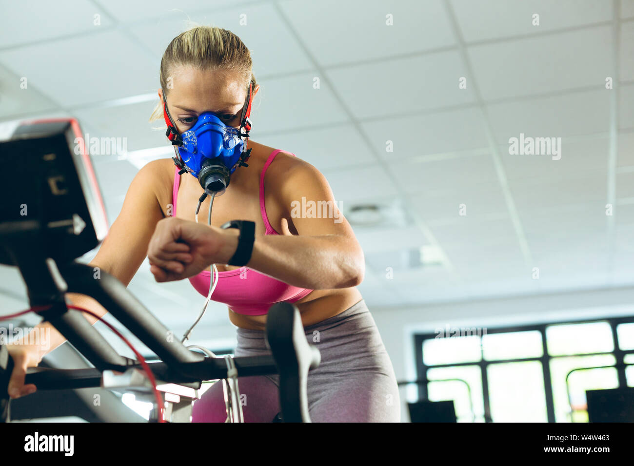 Female athlete with oxygen mask checking time while exercising with ...