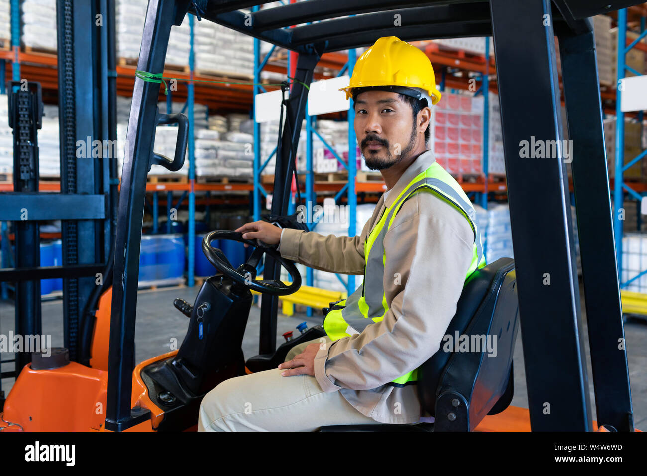 Male worker sitting in forklift and looking at camera in warehouse ...