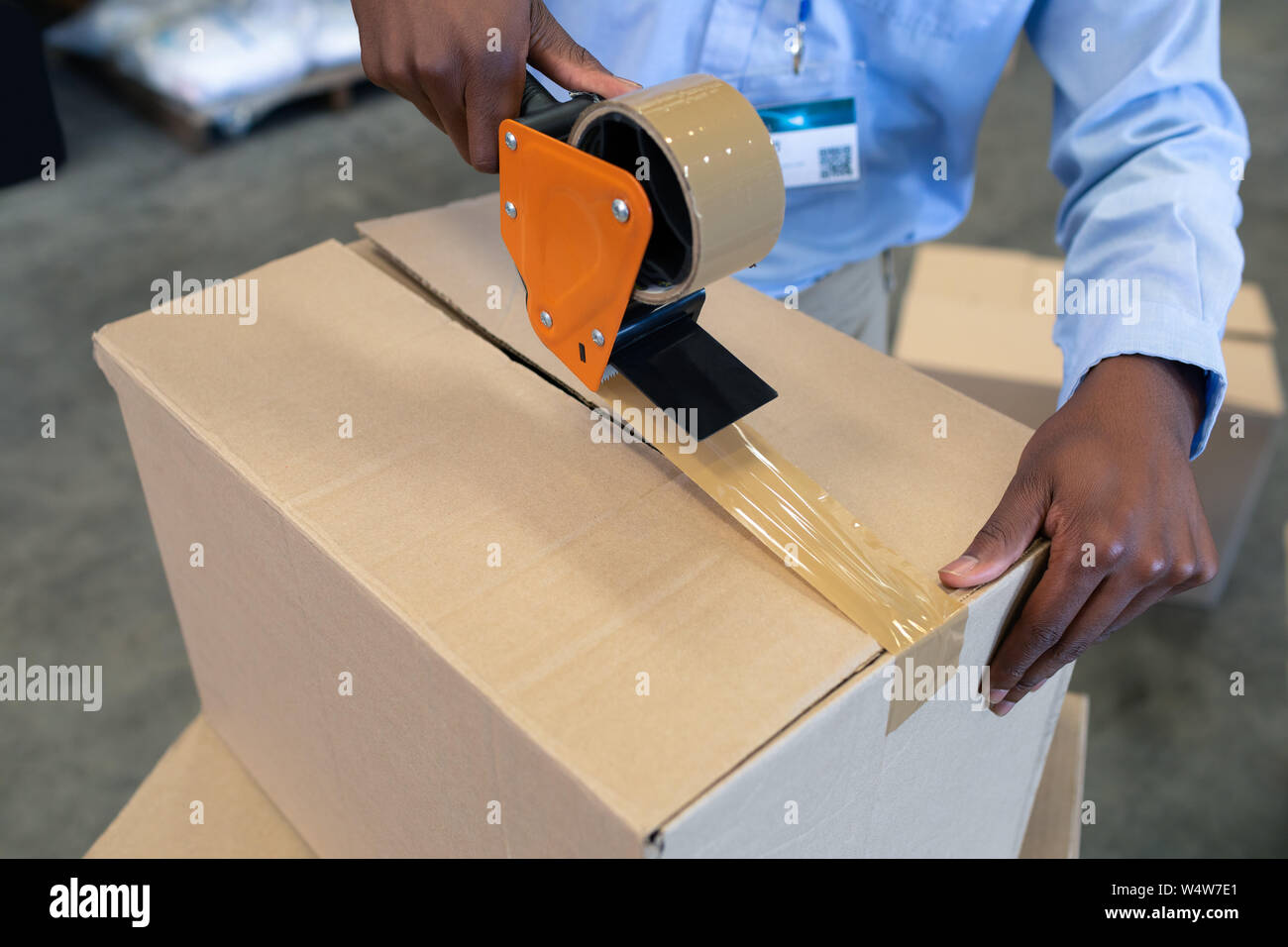 Male staff packing cardboard box with tape gun dispenser in warehouse ...