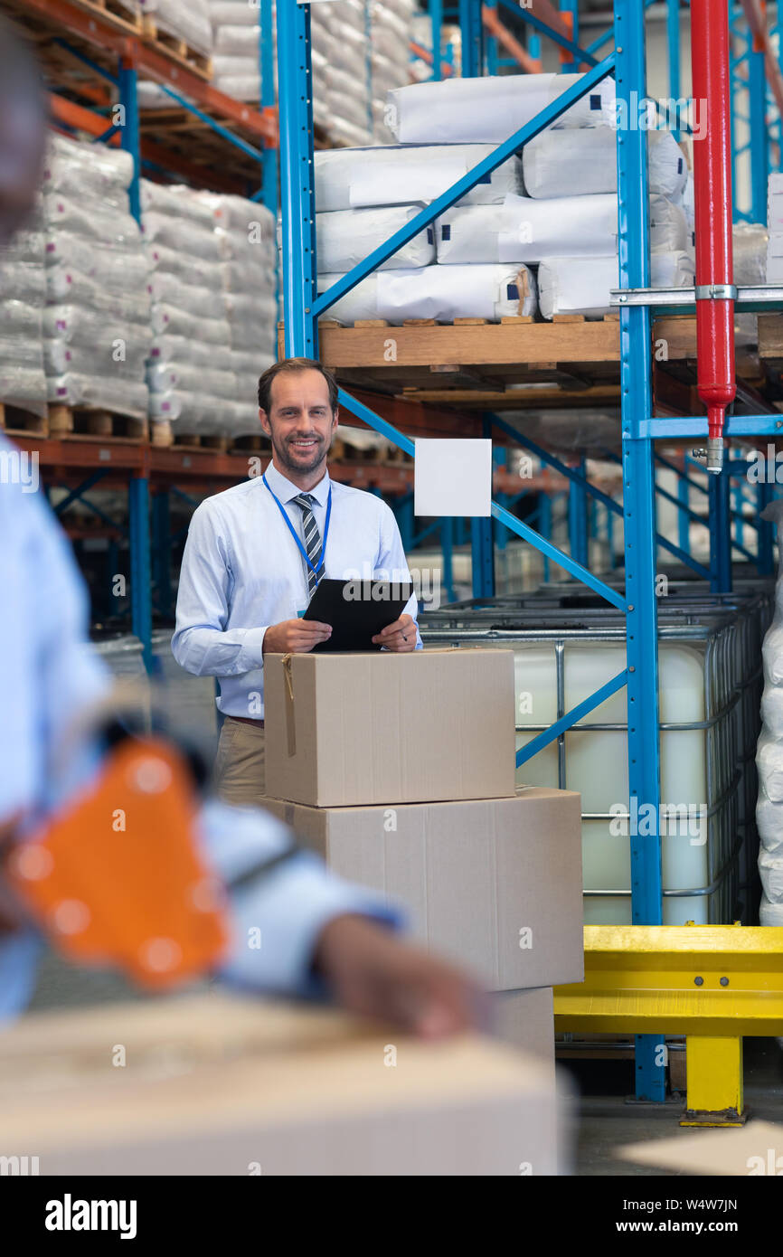 Male supervisor with clipboard looking at camera in warehouse Stock ...