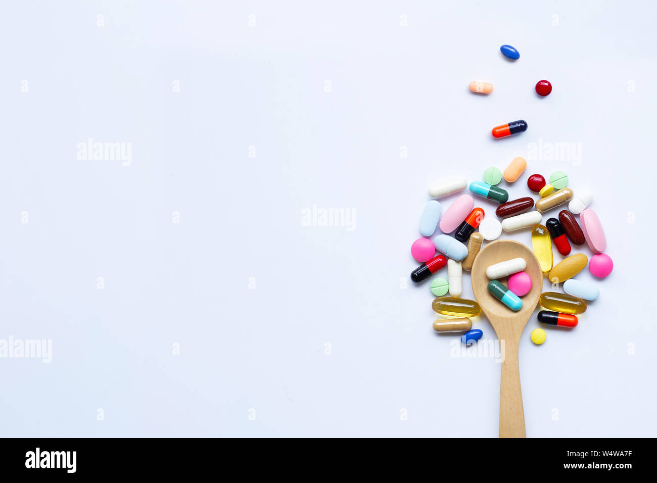 Colorful tablets, capsules and pills with wooden spoon on white ...
