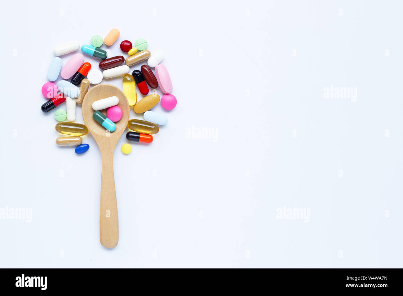 Colorful tablets, capsules and pills with wooden spoon on white ...