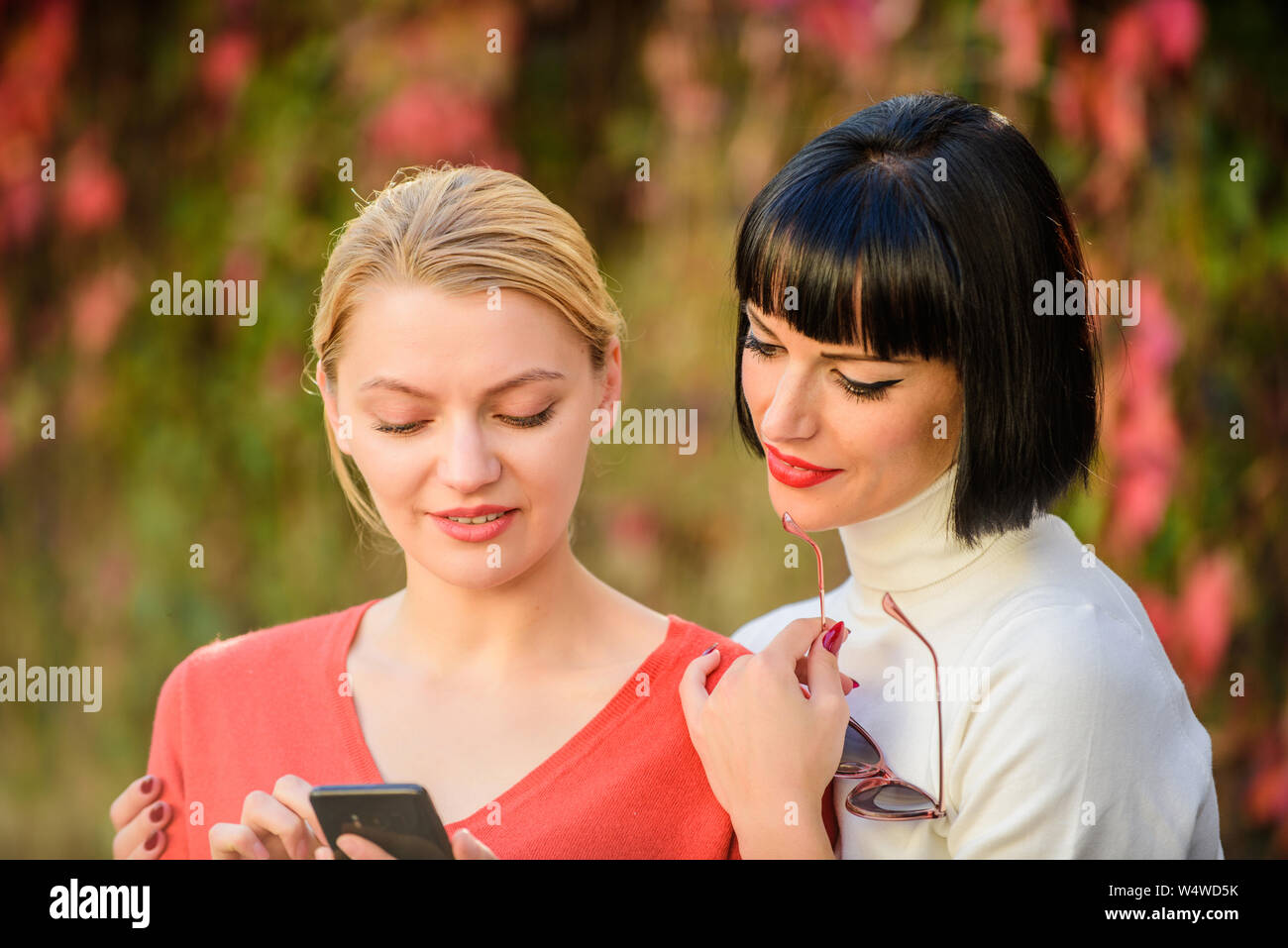 Two women with smartphone communicating outdoors. Sharing link. Buy ...