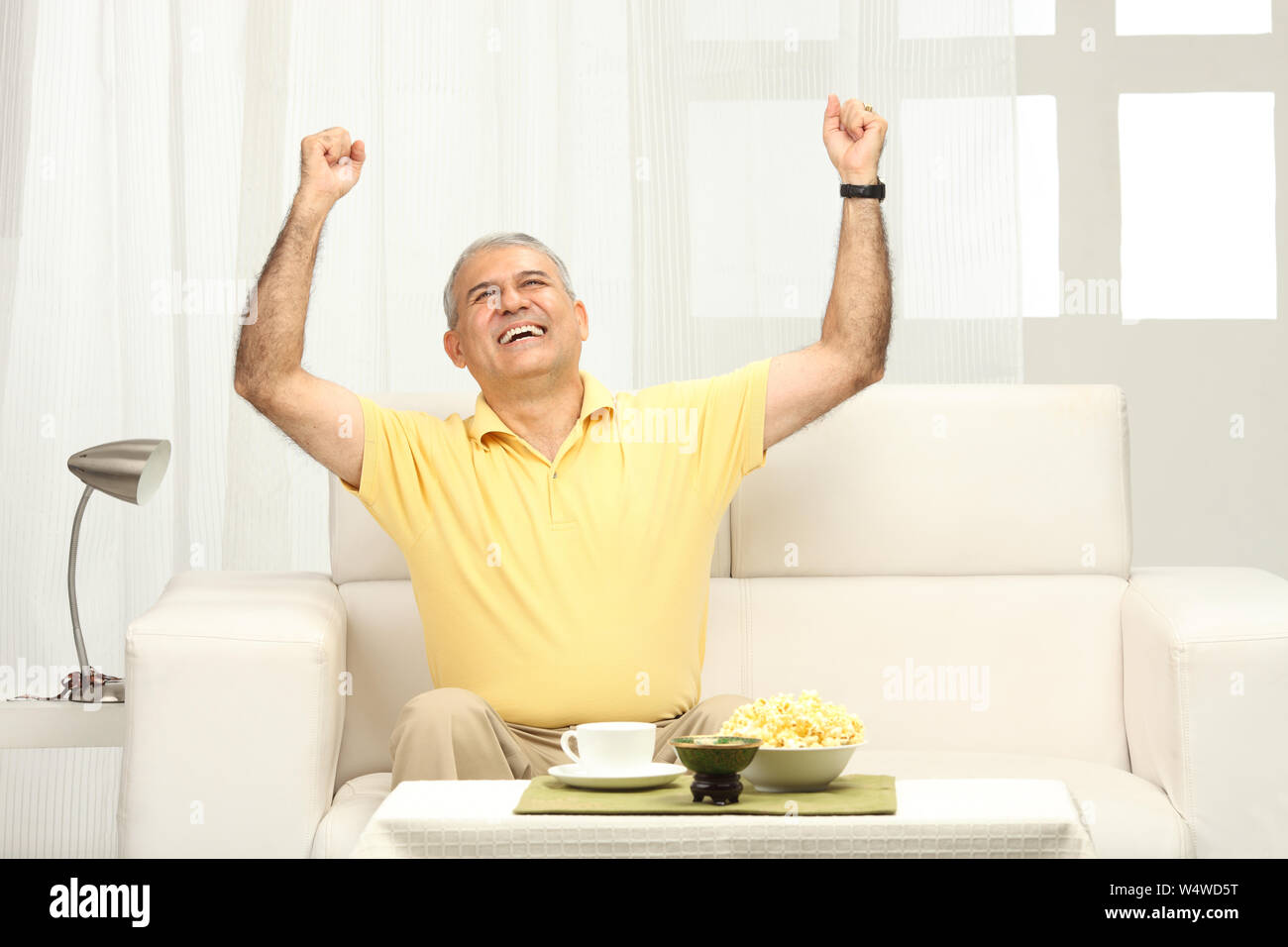 Man sitting on a couch and smiling his arms raised Stock Photo - Alamy