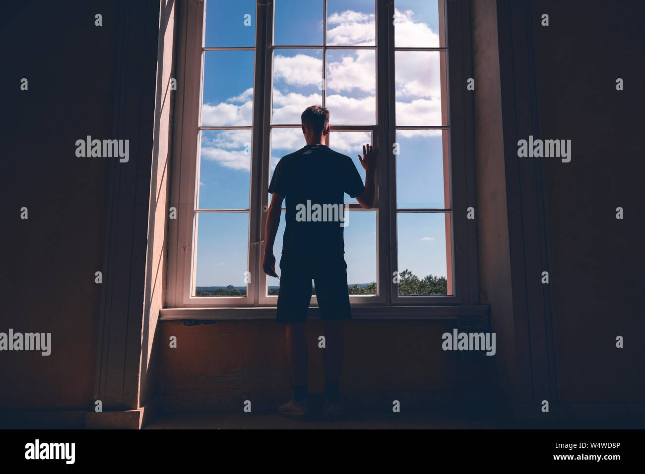 young man standing in a dark room in front of a window Stock Photo - Alamy