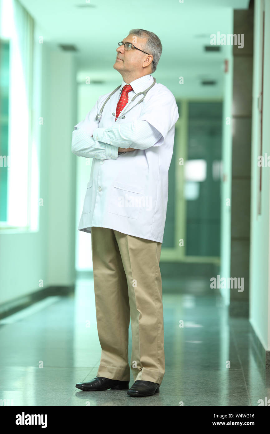 Male doctor standing with his arms crossed and thinking Stock Photo - Alamy