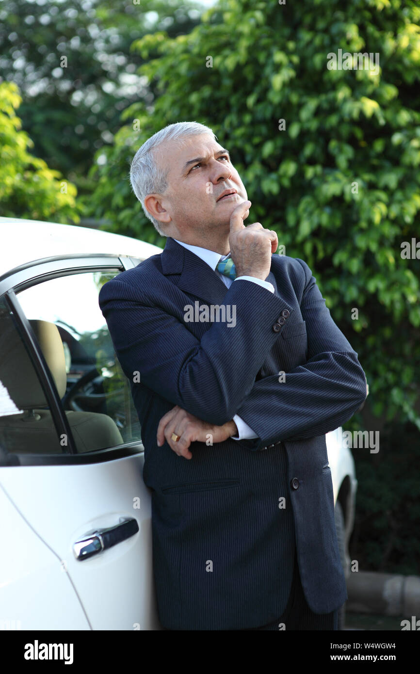 Businessman leaning back against car and thinking Stock Photo - Alamy