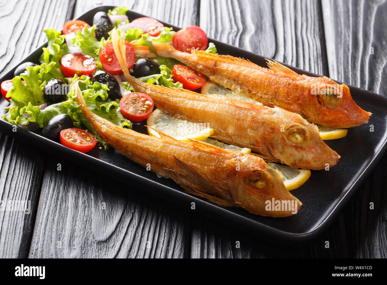 Portion of fried fish gurnard served with fresh vegetable salad and ...