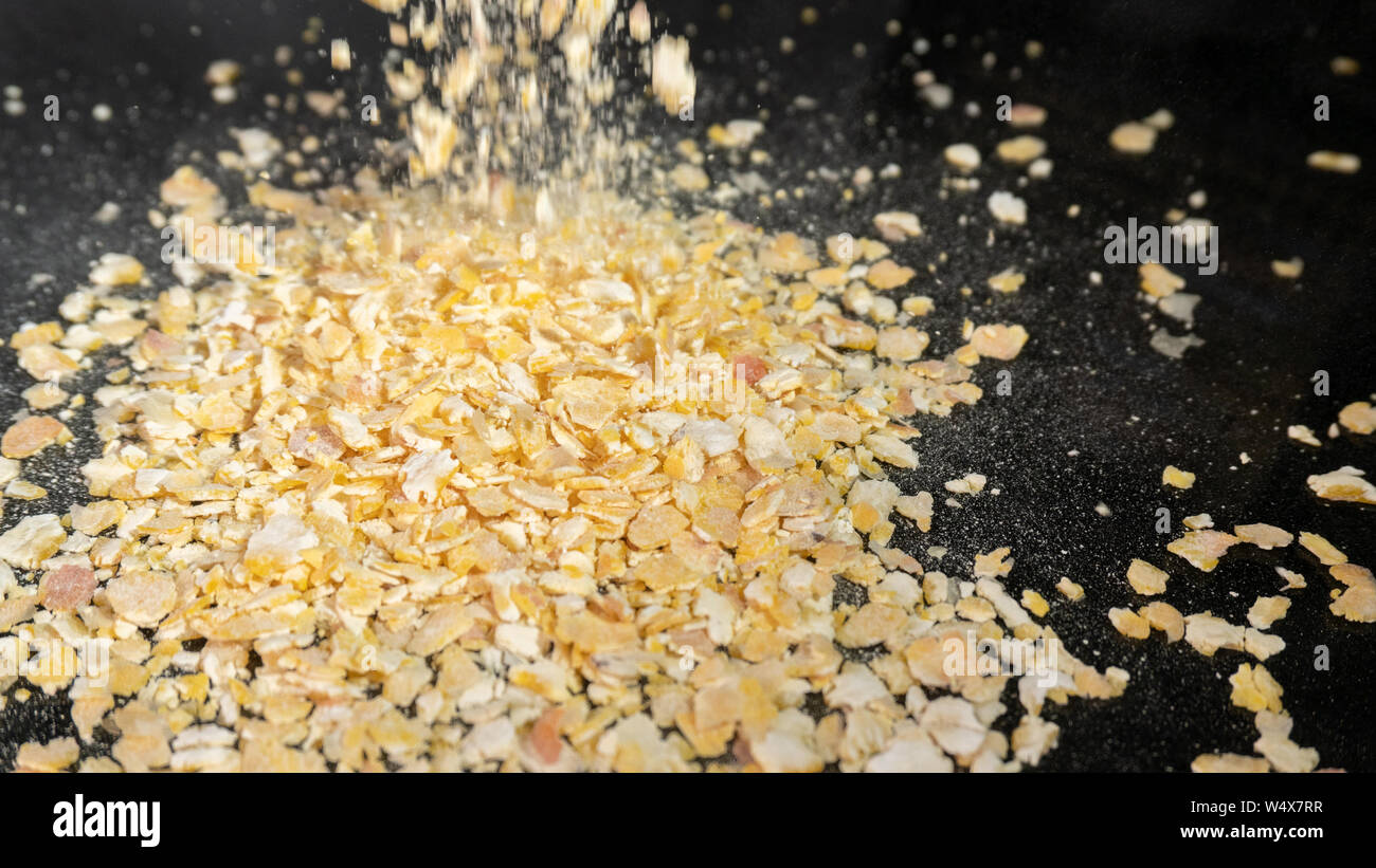 Corn flakes in a pile on a wooden board with new flakes falling out on ...