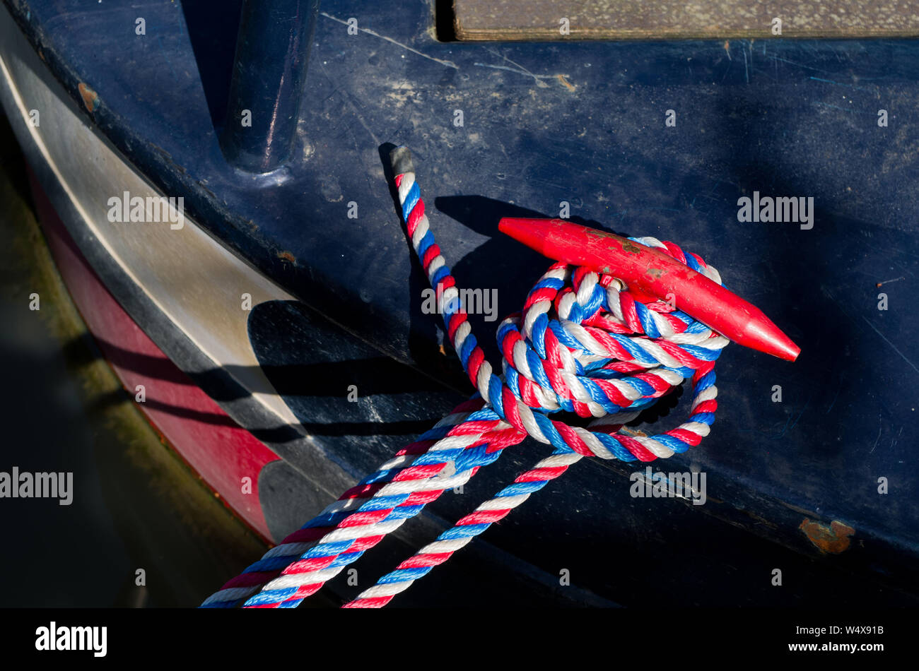 Close up of a red cleat and a striped rope securing a narrowboat to its ...