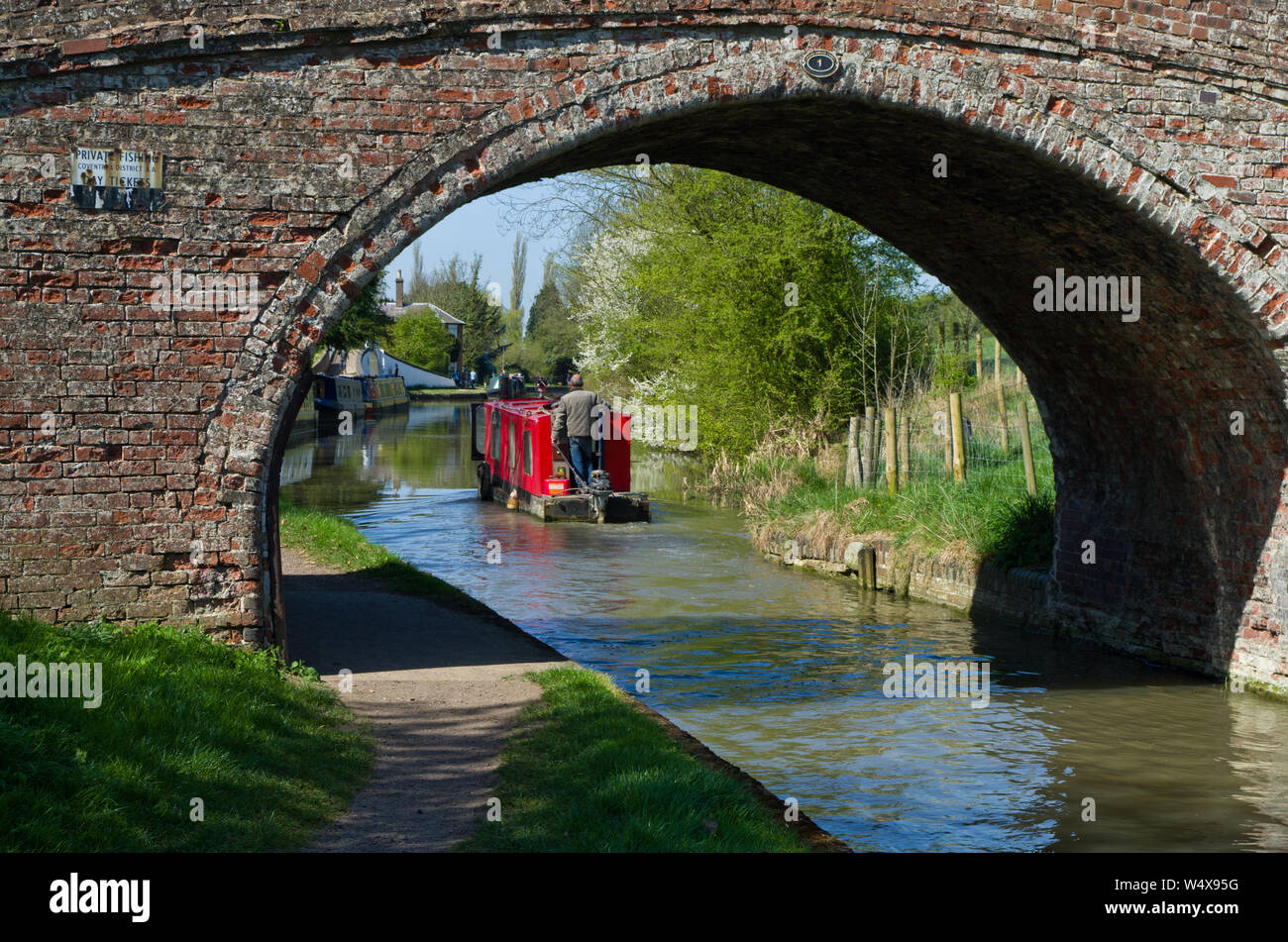 Red narrowboat passing under canal bridge No 1 on the Grand Union canal ...