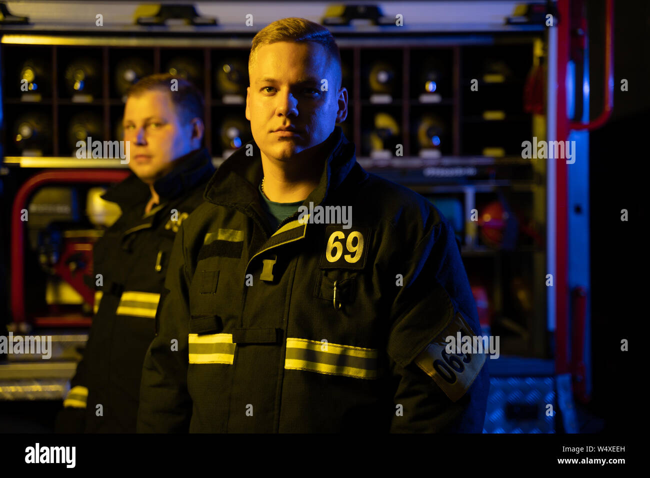 Image of two firefighter looking into camera near fire truck, neon ...