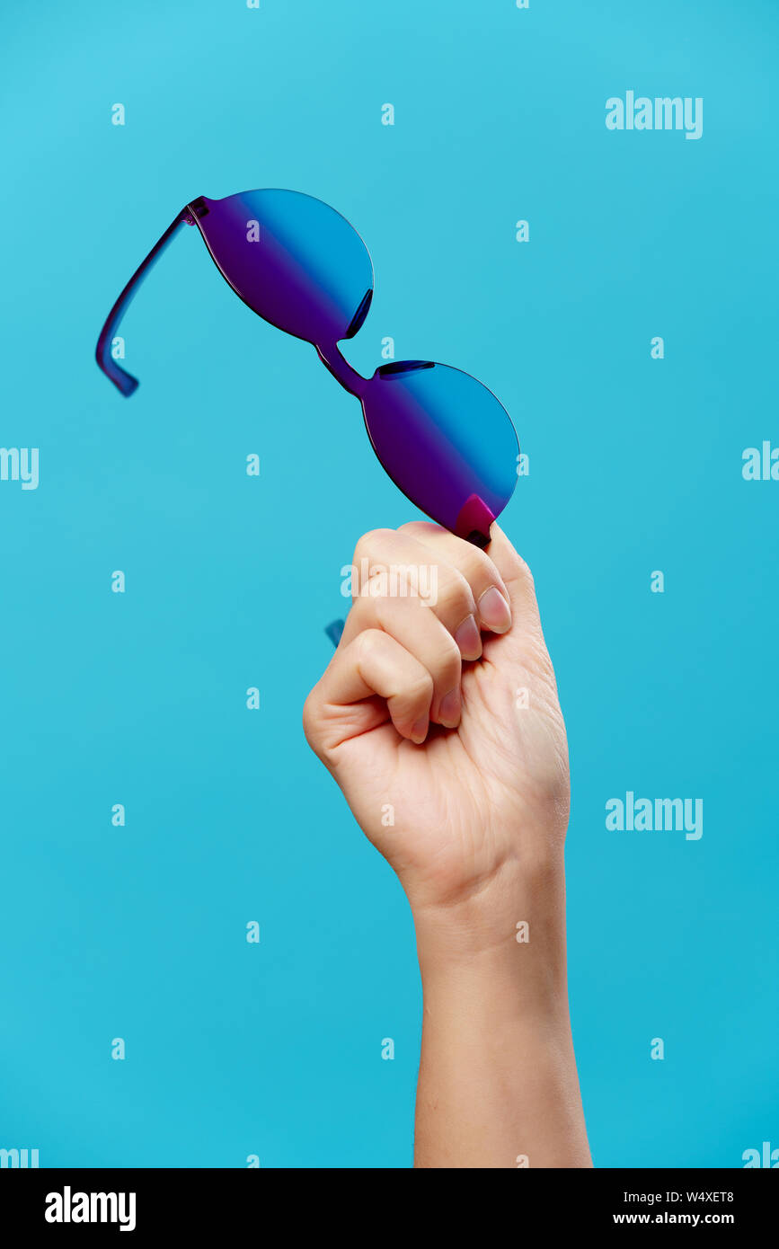 Photo of hand with sunglasses on empty blue background in studio Stock ...