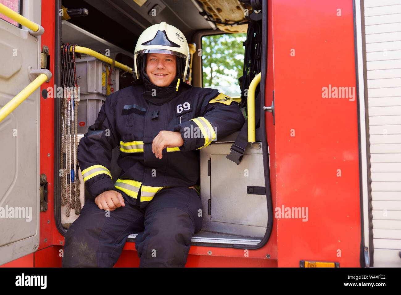 Photo of smiling fireman wearing helmet sitting in fire truck at fire ...