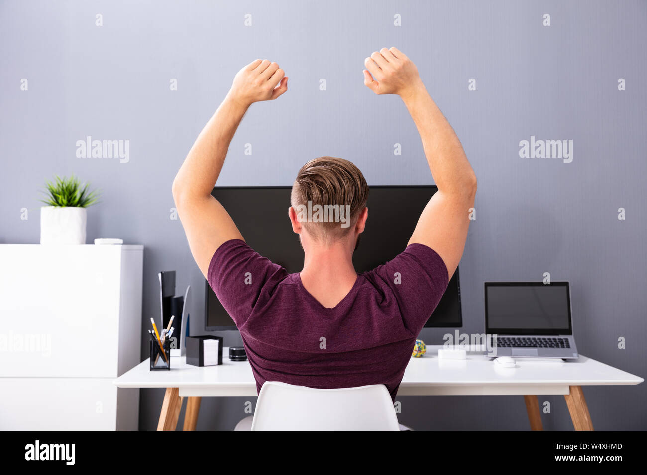 Rear View Of Businessman Sitting On Chair With Arm Raised In Office ...