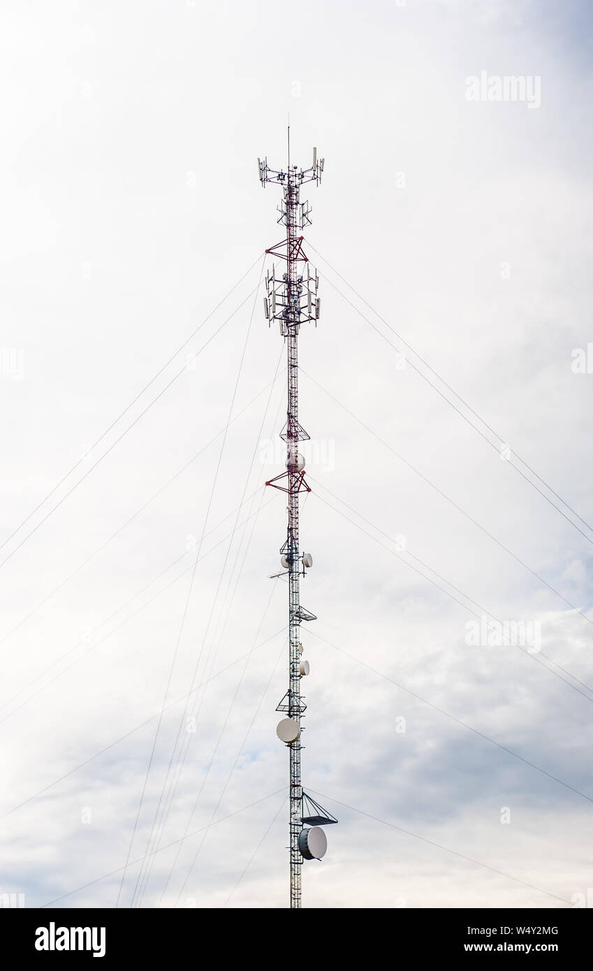 Tall red and white metal communications antenna tower with dishes and supporting cables, against ...