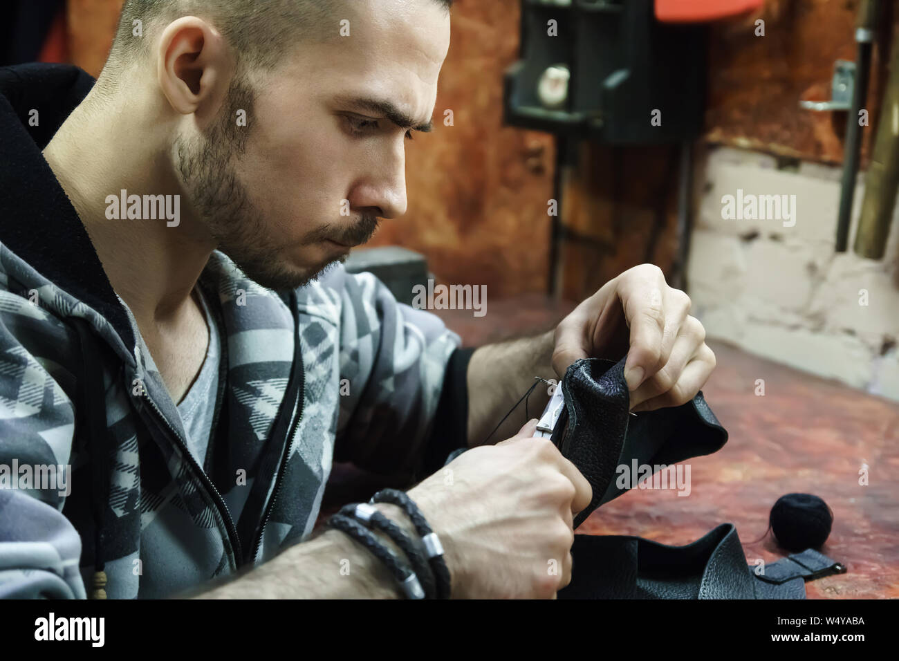 Craftsman intently works with leather. Tanner sews leather goods ...
