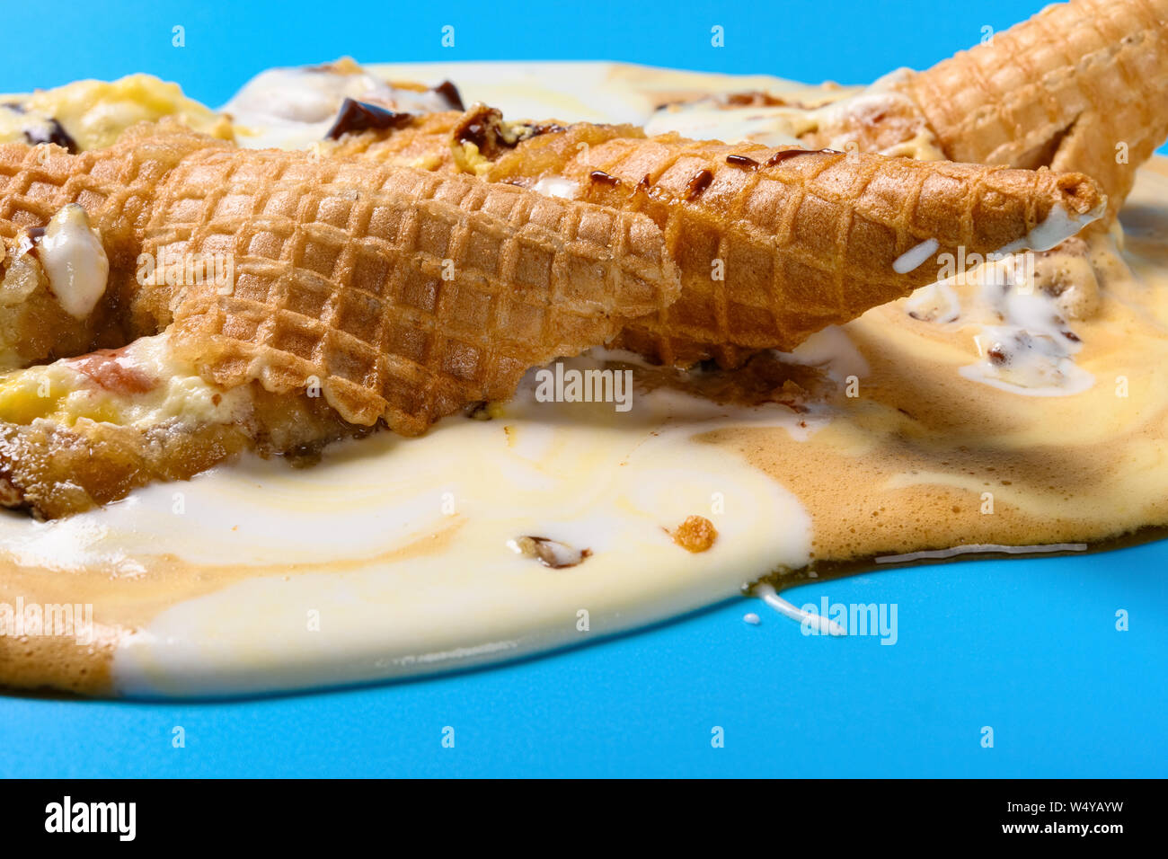 side view multiple flavor ice cream cones melted on blue background ...