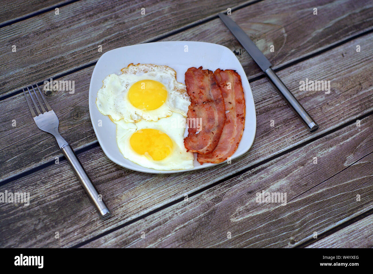 Traditional breakfast, plate with fried eggs and bacon and cutlery next ...