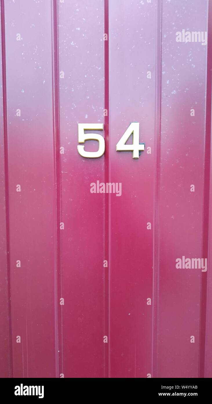 The number 54 is golden in color on a red metal corrugated surface ...