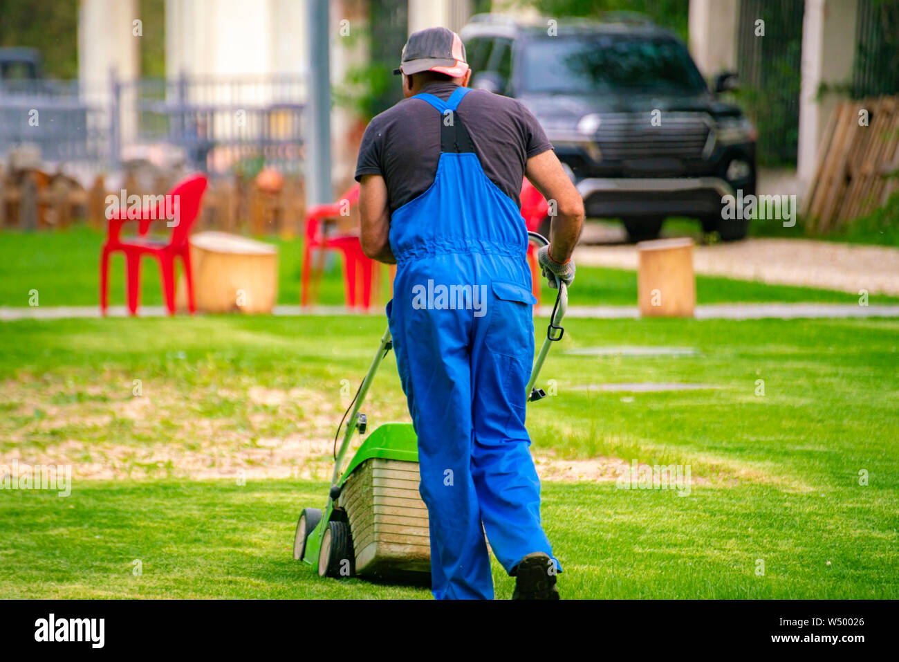 gardener worker cutting grass with mower in the backyard lawn field ...